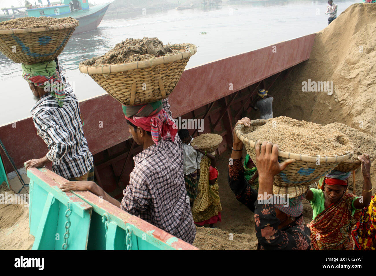 Male and female laborers carry heavy loads of sand balanced on their ...
