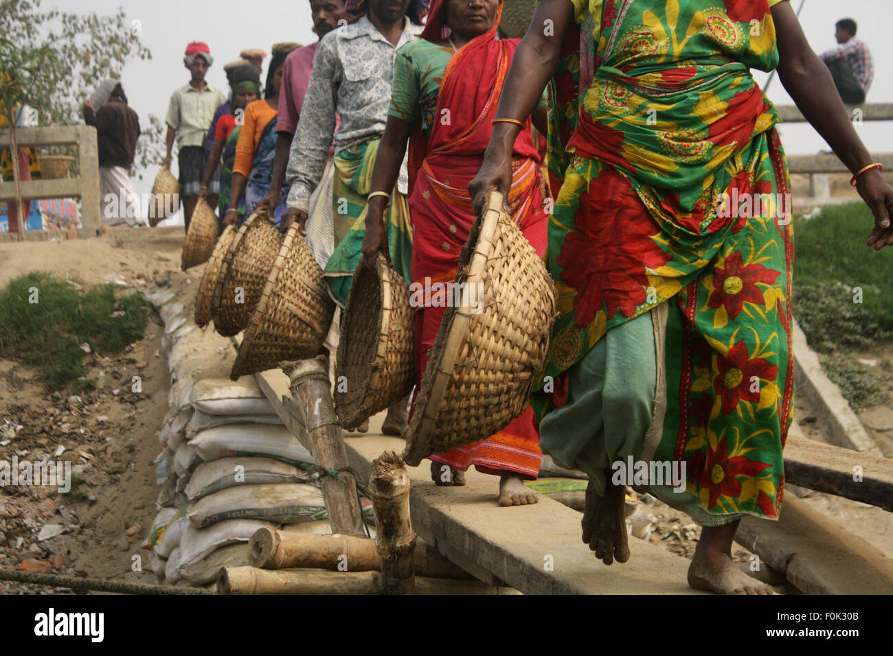 Male and female laborers carry heavy loads of sand balanced on their ...