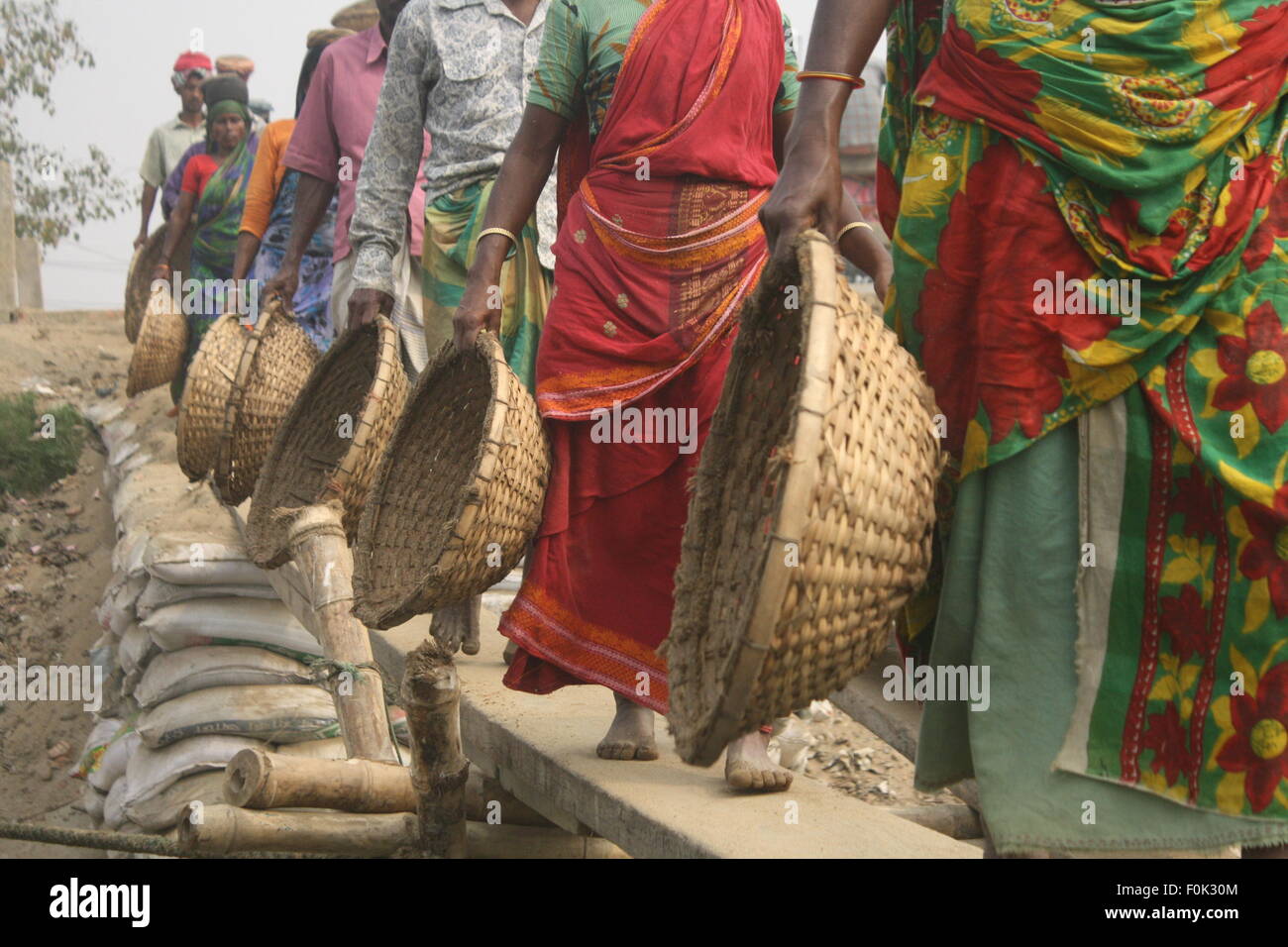 Male and female laborers carry heavy loads of sand balanced on their ...