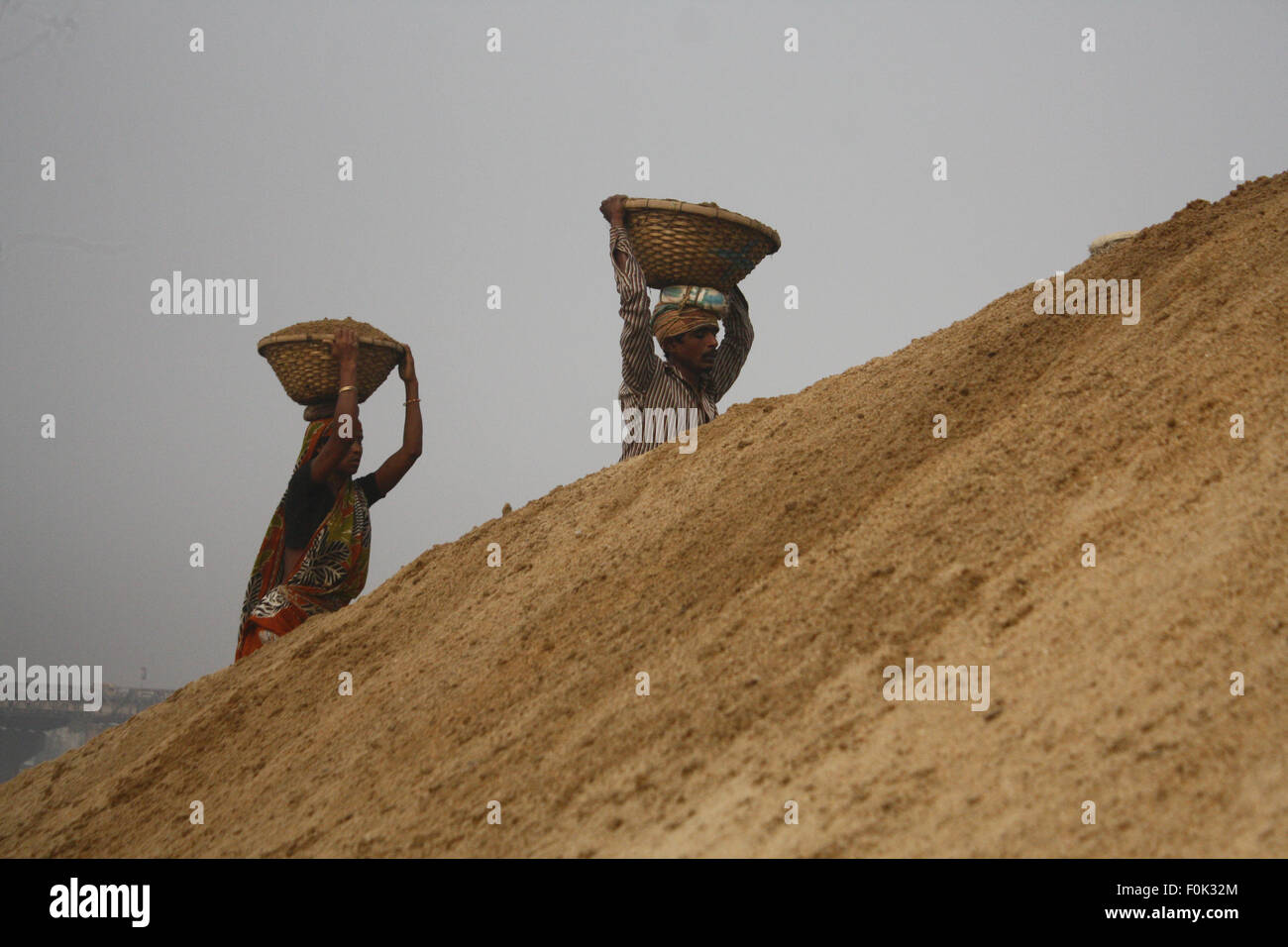 Male and female laborers carry heavy loads of sand balanced on their ...