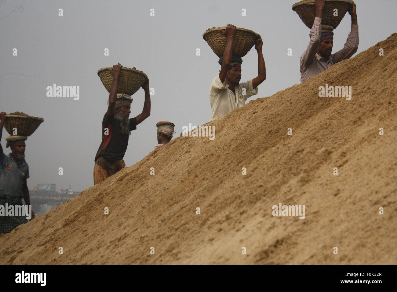 Male and female laborers carry heavy loads of sand balanced on their ...