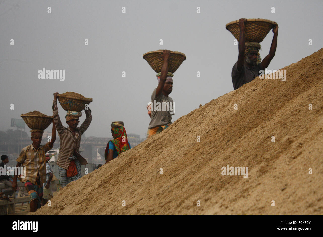 Male and female laborers carry heavy loads of sand balanced on their ...