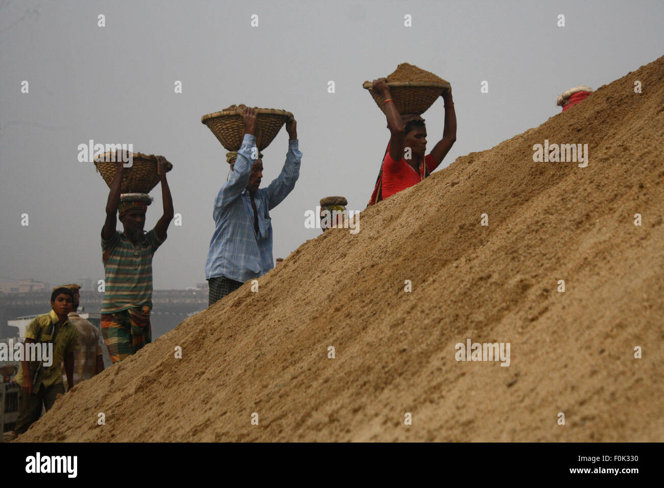 Male and female laborers carry heavy loads of sand balanced on their ...