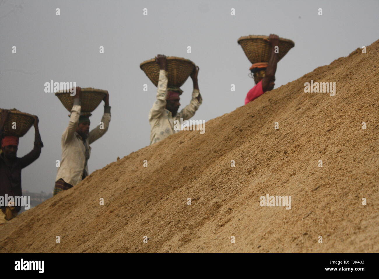 Male and female laborers carry heavy loads of sand balanced on their ...