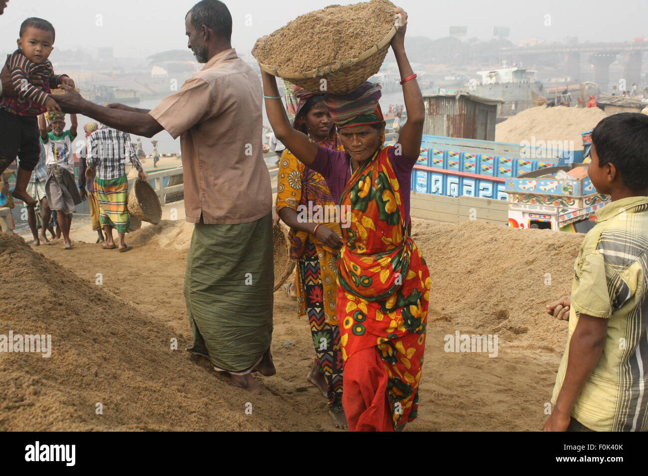 Male and female laborers carry heavy loads of sand balanced on their ...
