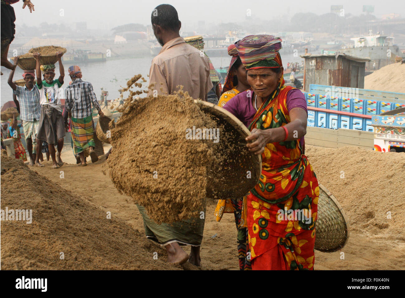 Male and female laborers carry heavy loads of sand balanced on their ...