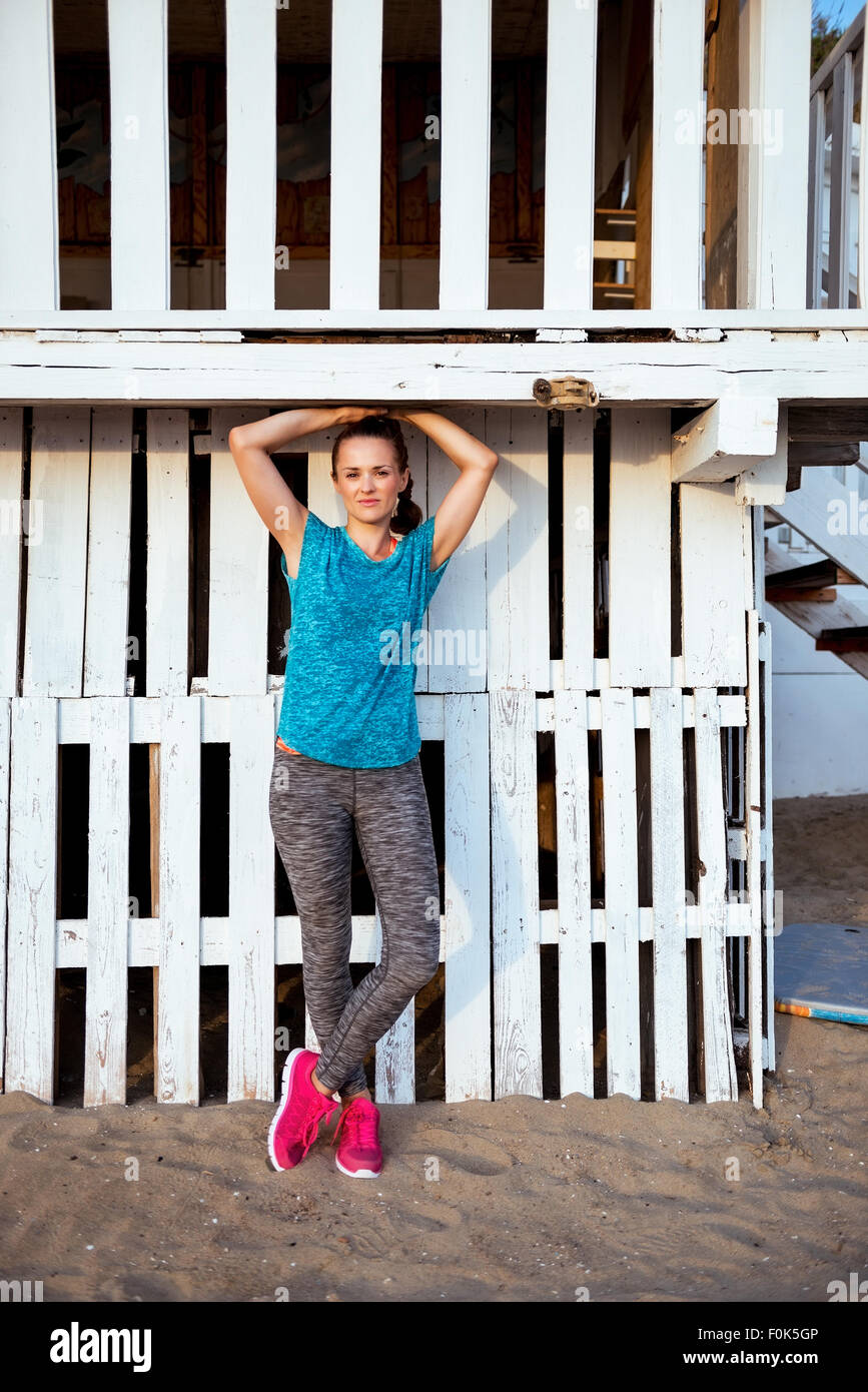 A woman stands casually under a beach house, legs crossed, and arms ...