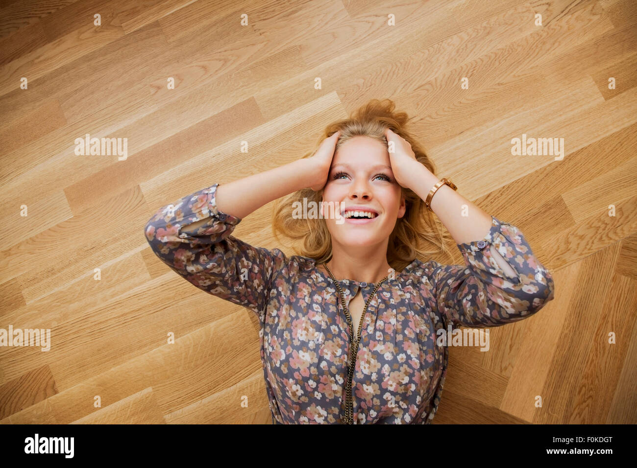 Top view of smiling young woman lying on floor holding her head Stock ...