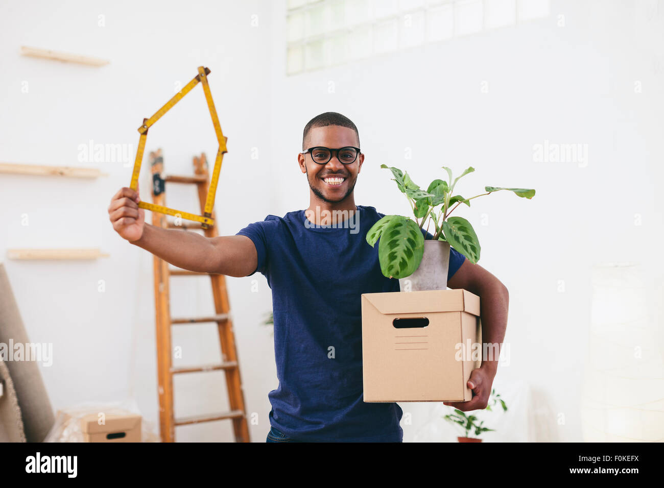 Smiling young man holding cardboard box and pocket rule shaped like a ...