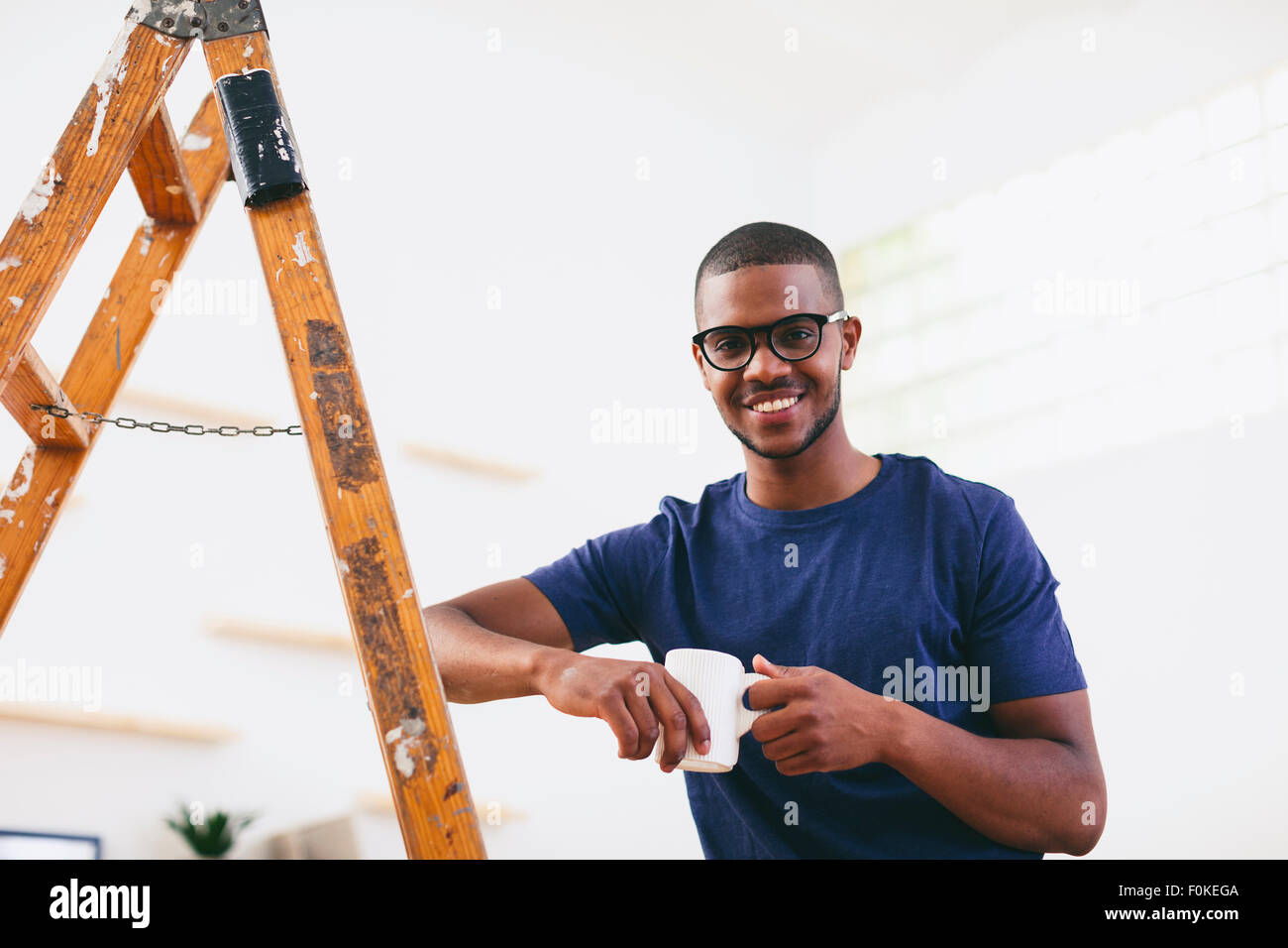 Smiling young man leaning on step ladder having a coffee break Stock ...