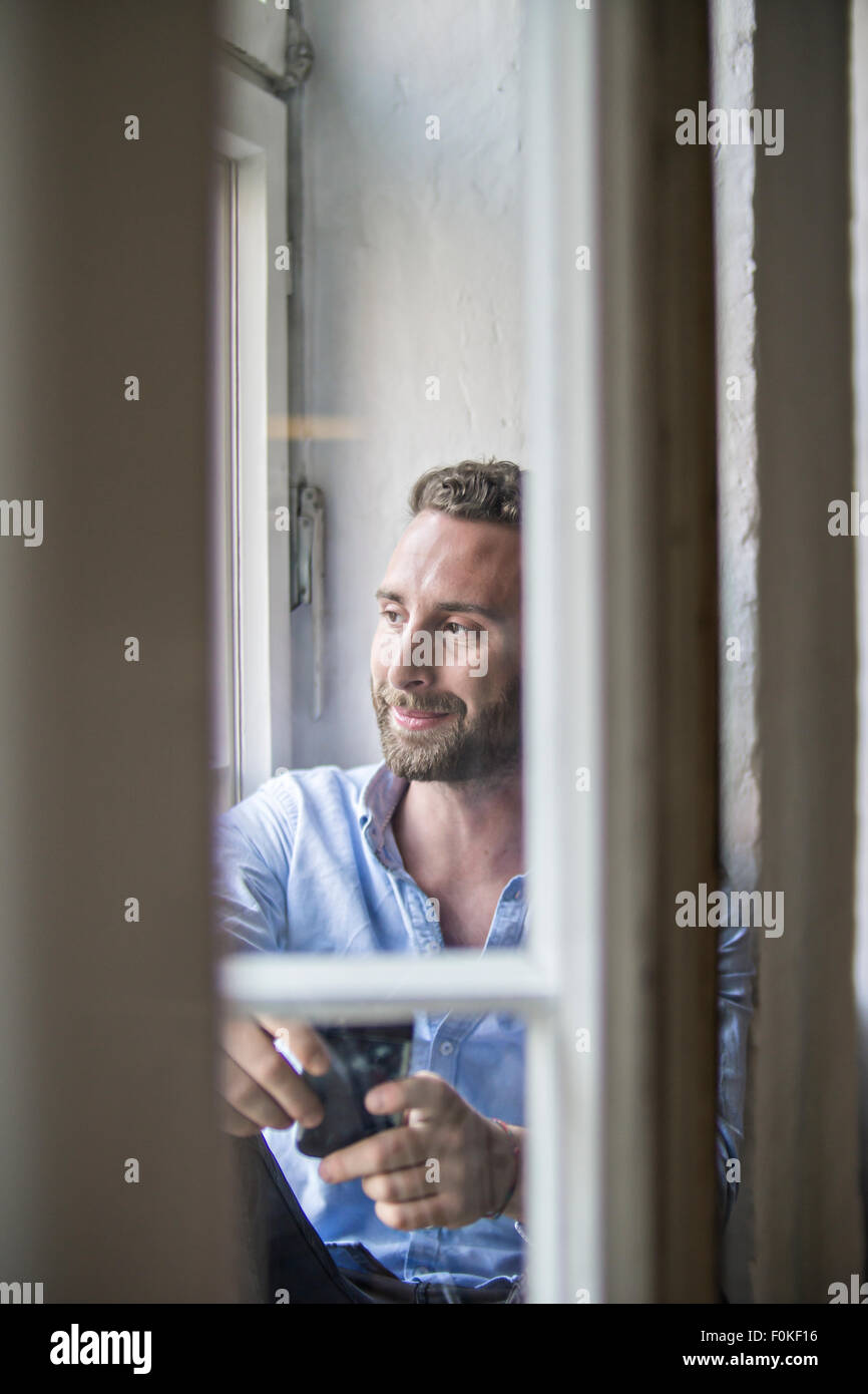 Smiling young man looking out of window Stock Photo - Alamy