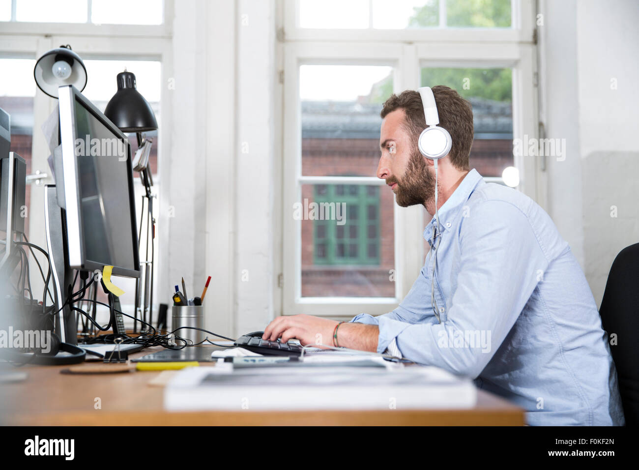 Young man in office wearing headphones working on computer Stock Photo ...
