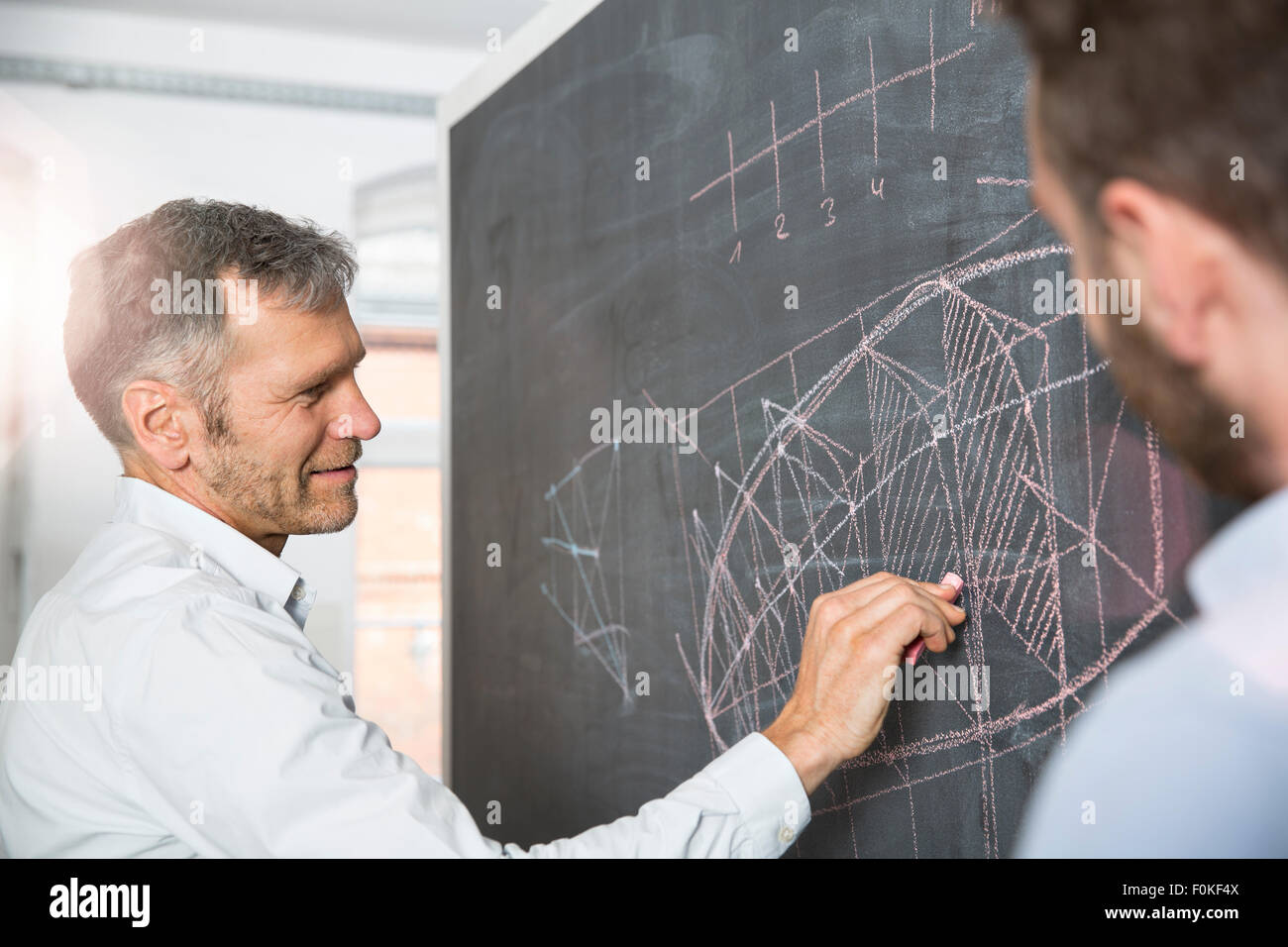 Businessman drawing at blackboard with colleague watching Stock Photo ...