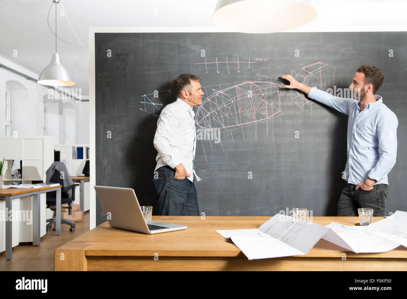 Two businessmen discussing drawing at blackboard Stock Photo - Alamy