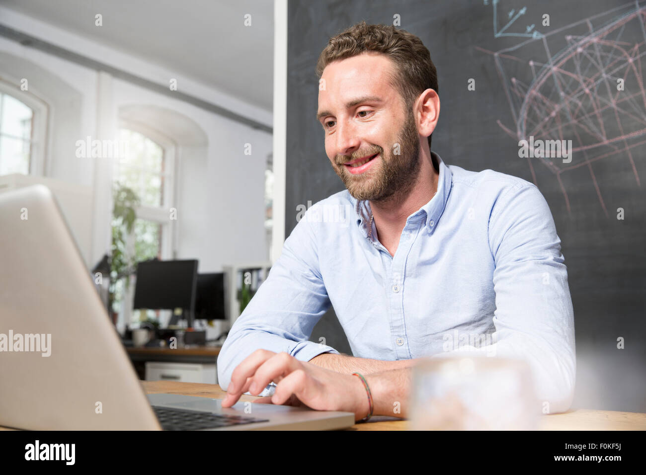Young man in office using laptop Stock Photo - Alamy