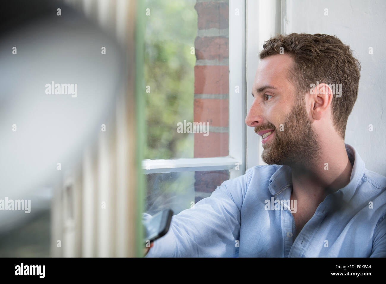 Smiling young man looking out of the window Stock Photo - Alamy