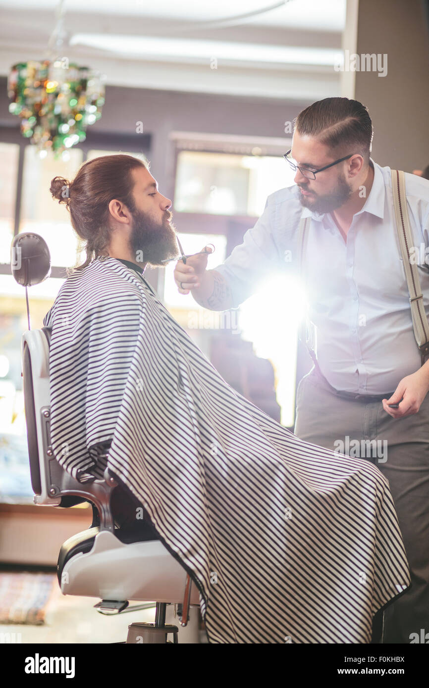 Barber cutting beard of a customer Stock Photo - Alamy