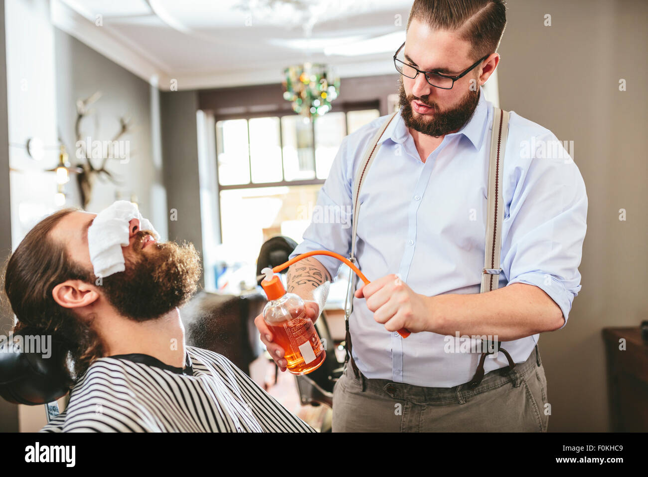 Barber spraying aftershave on beard of a customer Stock Photo - Alamy