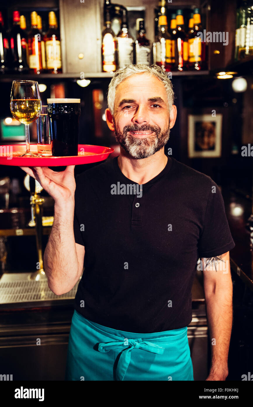 Portrait of smiling waiter holding tray with beverages in an Irish pub ...