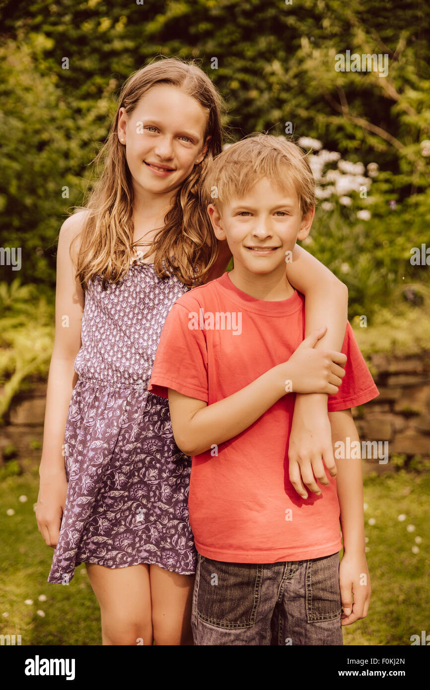 Smiling girl putting arm around brother in garden Stock Photo - Alamy