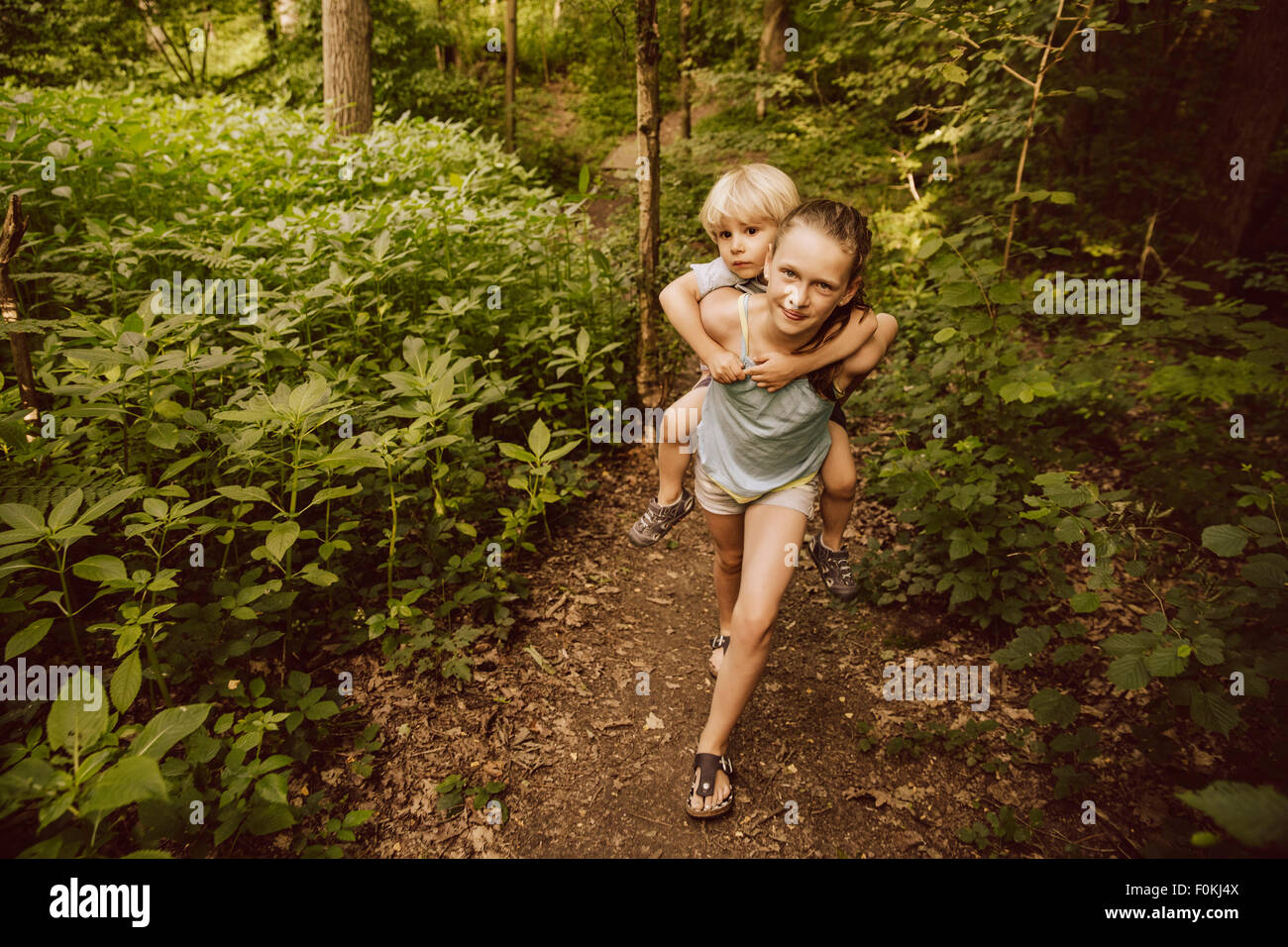 Girl carrying little boy piggyback through a forest Stock Photo - Alamy