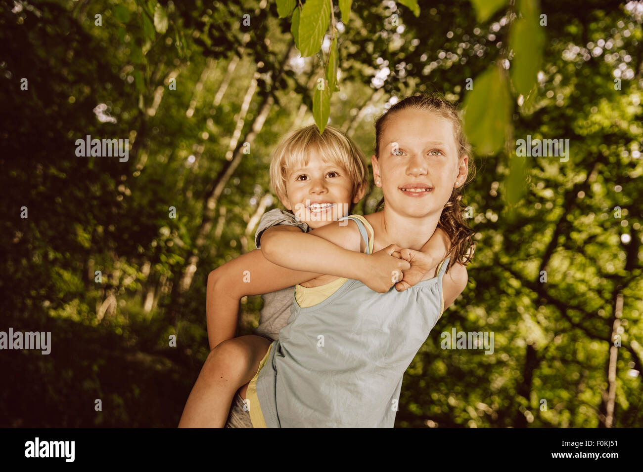 Girl carrying little boy piggyback through a forest Stock Photo - Alamy