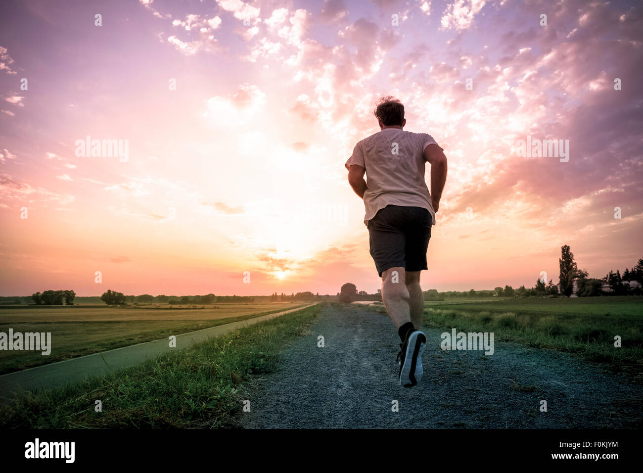 Rear view of man jogging at sunset Stock Photo - Alamy