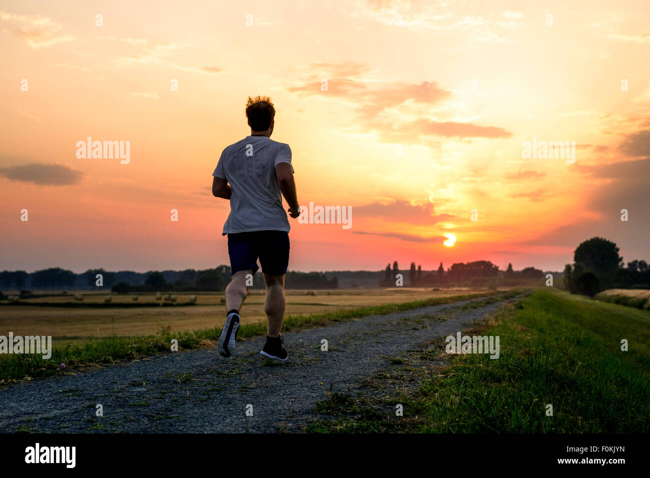 Rear view of man jogging at sunset Stock Photo - Alamy