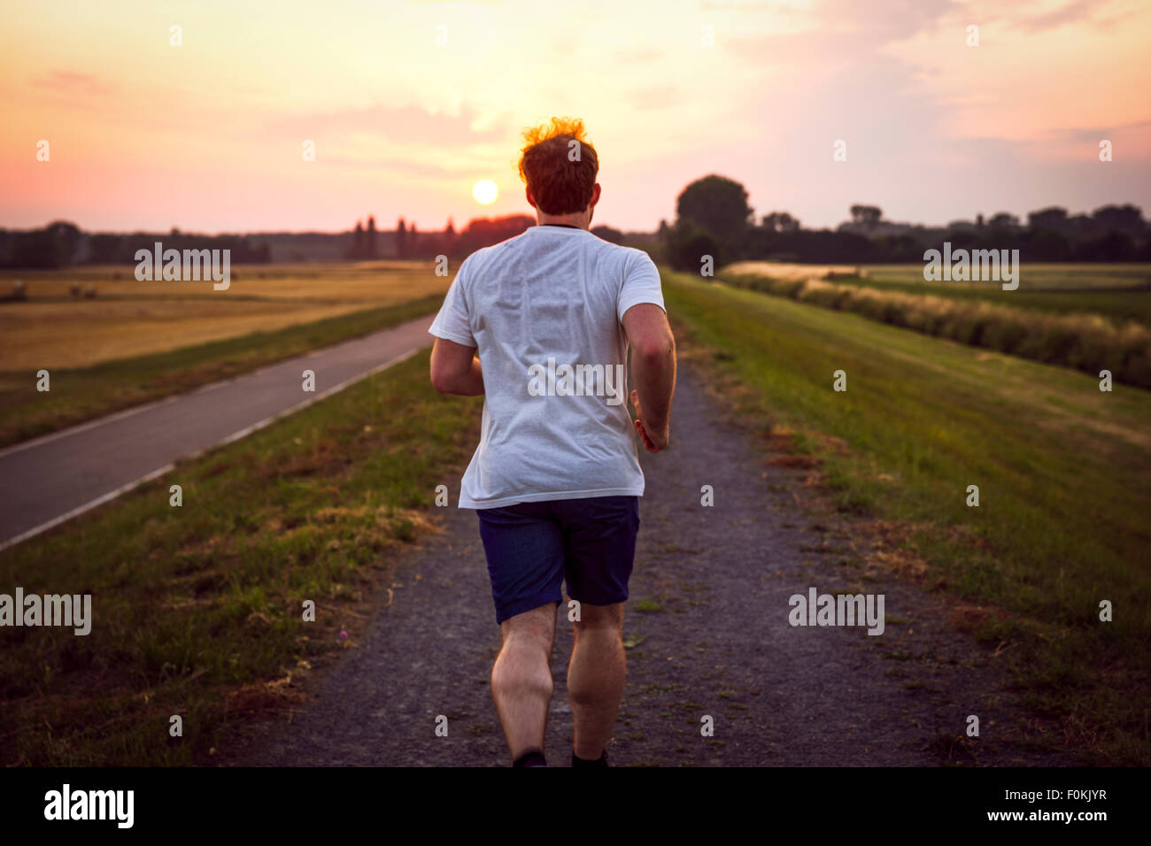 Rear view of man jogging at sunset Stock Photo - Alamy