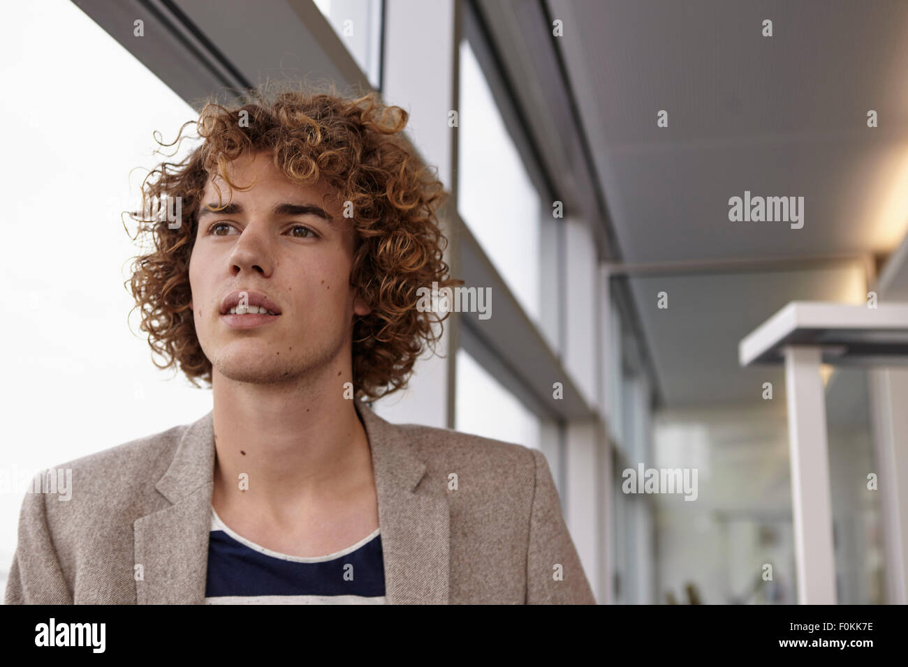 Young man with curly hair looking out of window Stock Photo - Alamy