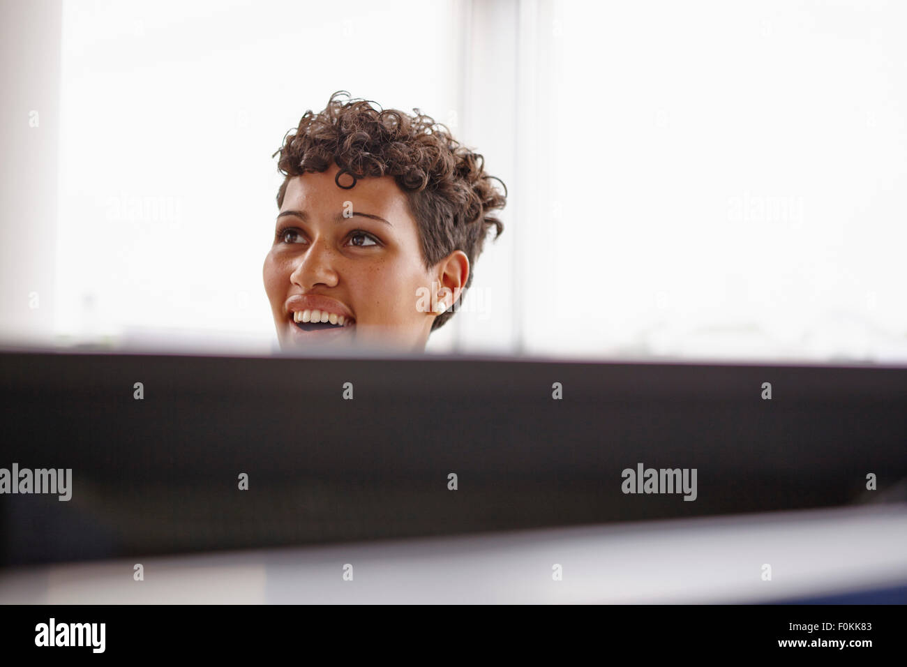 Smiling young woman in office behind computer screen Stock Photo - Alamy