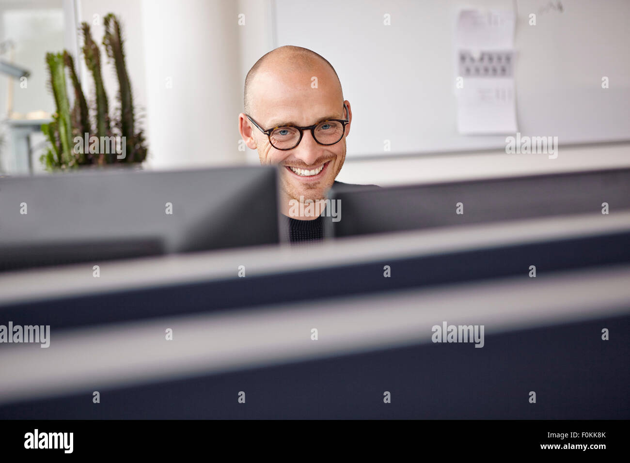 Smiling man in office behind computer screens Stock Photo - Alamy