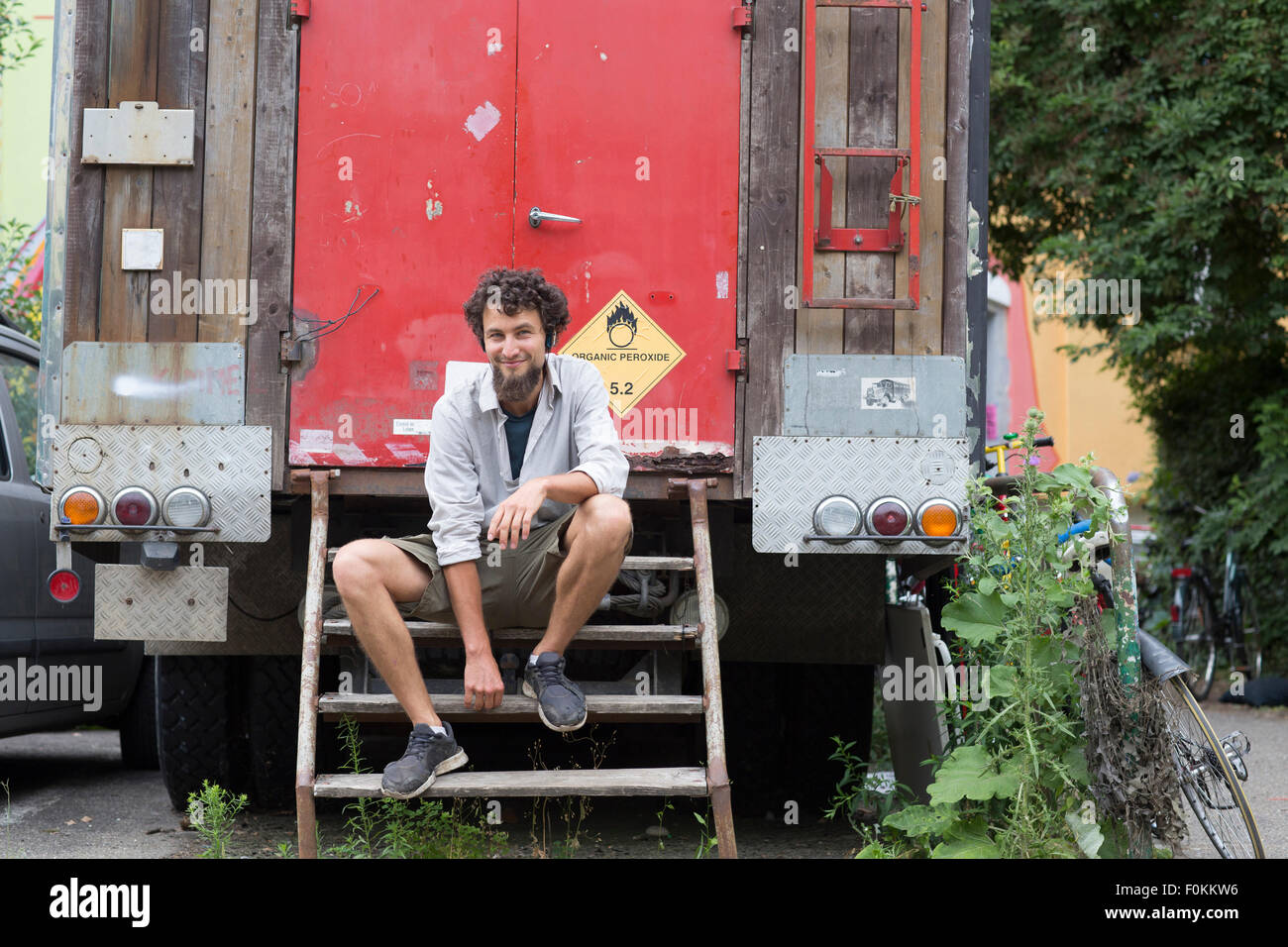 Smiling young man sitting on stairs of a trailer Stock Photo - Alamy