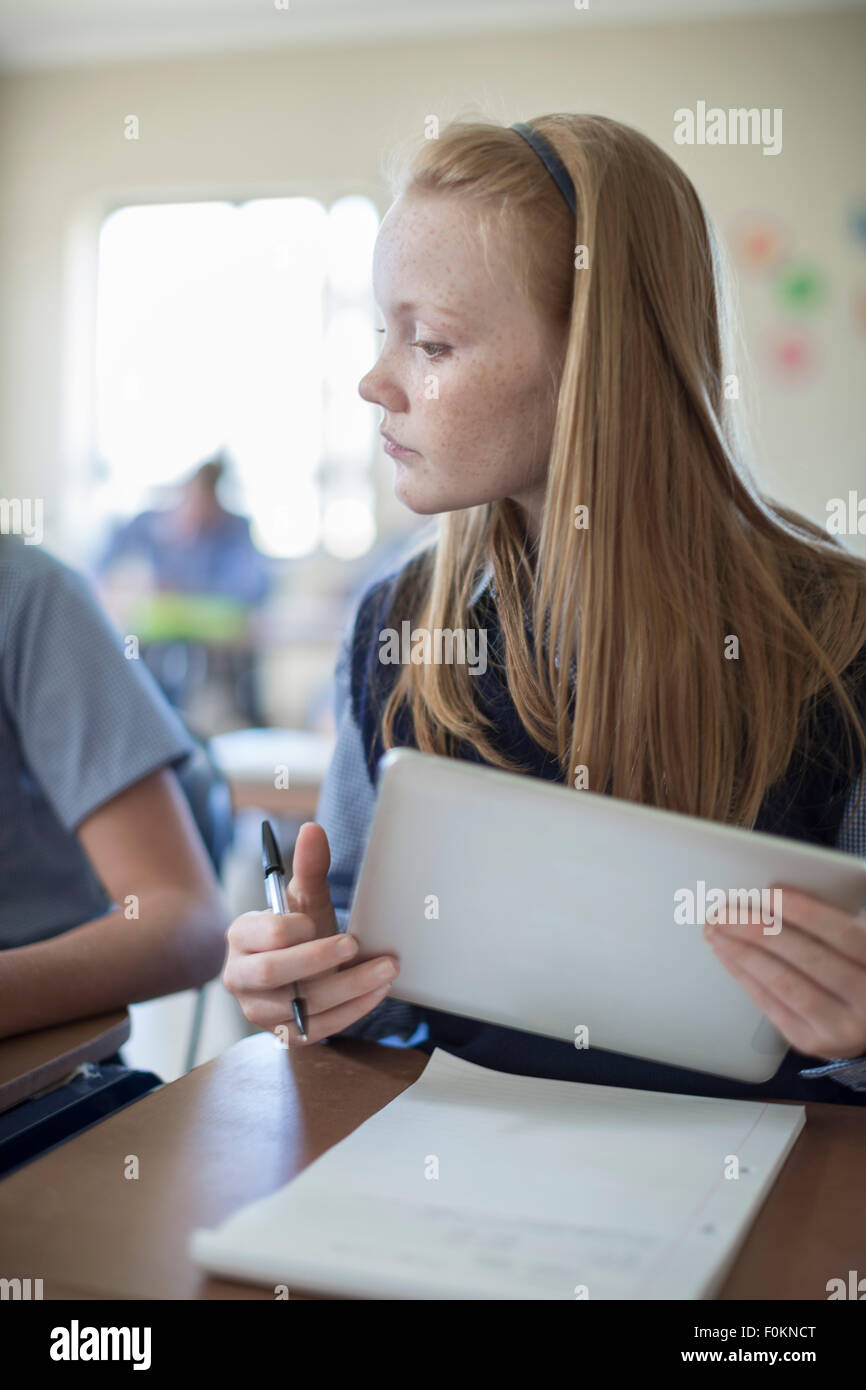 Schoolgirl in classroom with digital tablet looking to classmate Stock ...