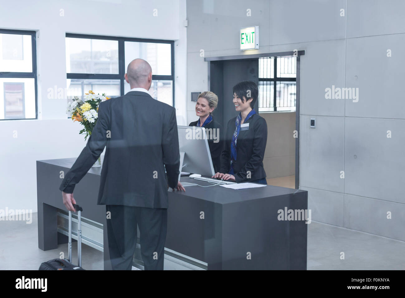 Two women behind reception desk in hotel lobby helping businessman ...