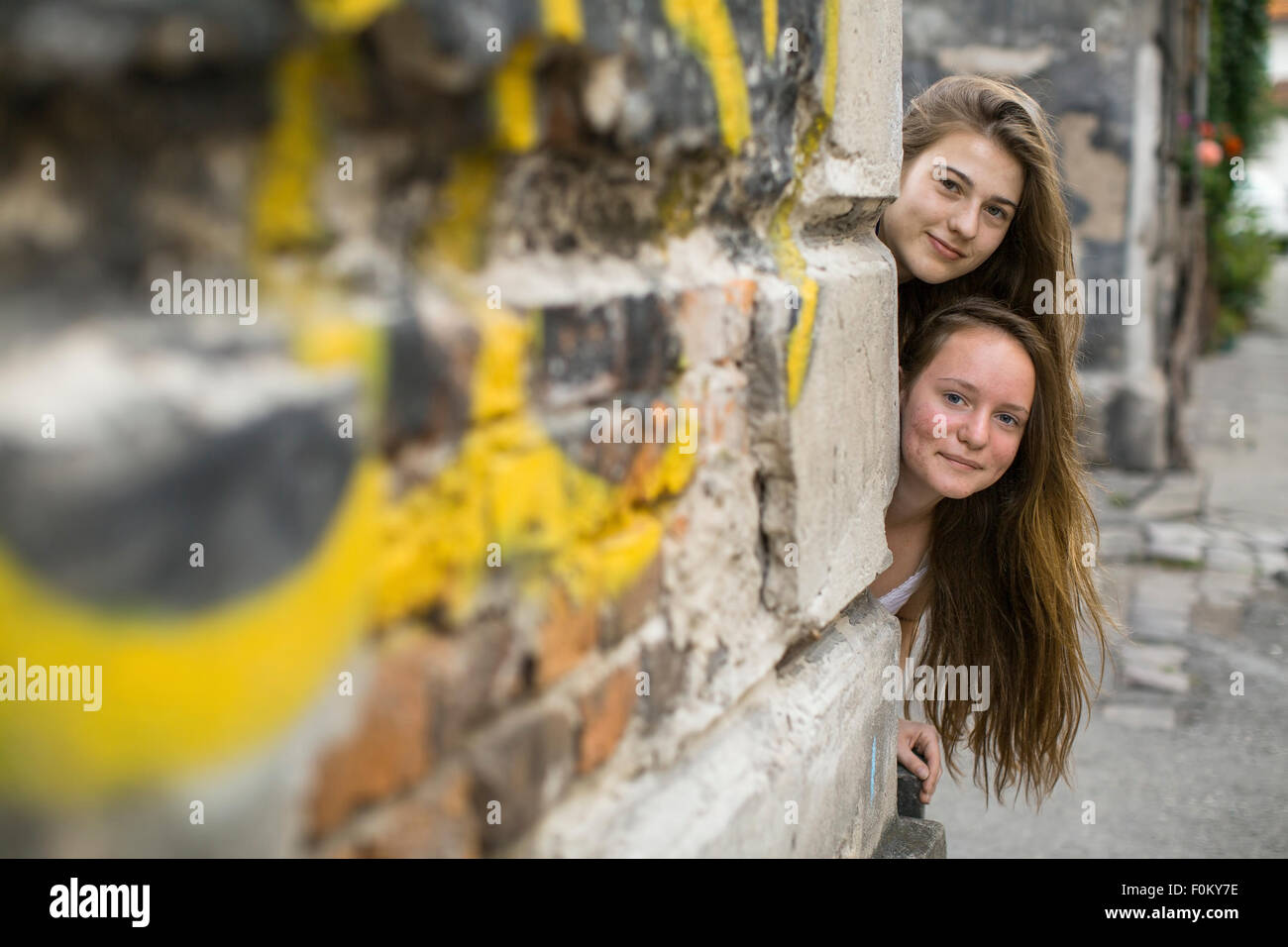 Two teenage girls look out behind the corner of the house Stock Photo ...