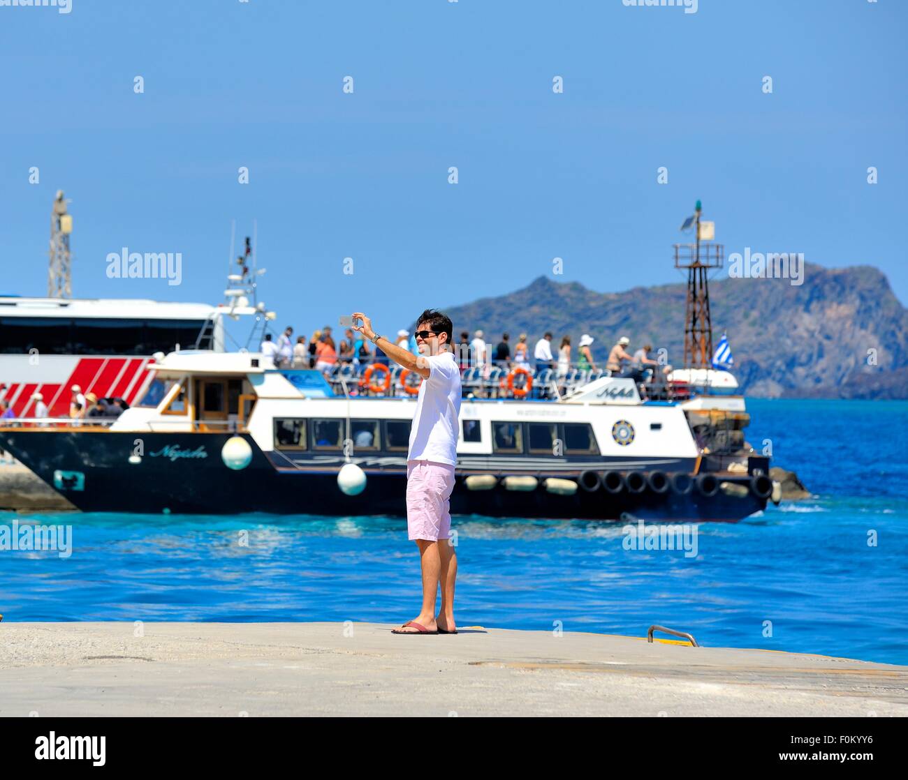 A man taking a selfie with a mobile phone in the port Ormos Athinios ...