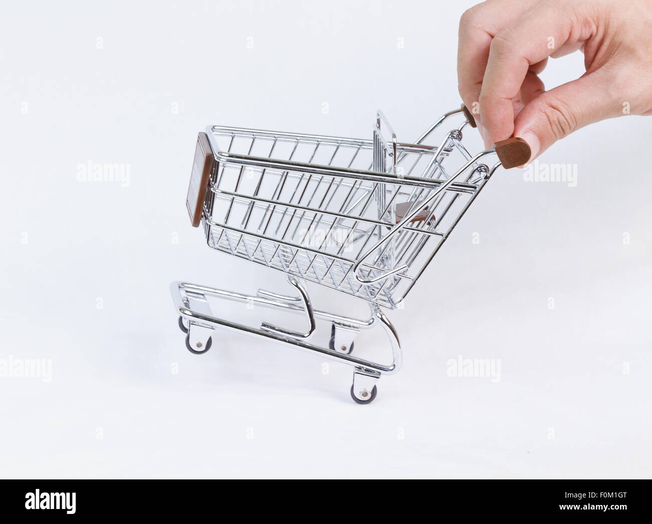 Hand pushing a tilted wire frame shopping cart with brown trim isolated ...