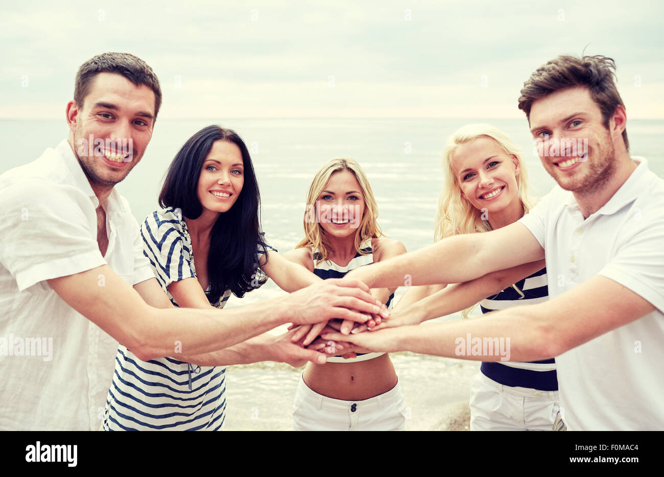smiling friends putting hands on top of each other Stock Photo - Alamy