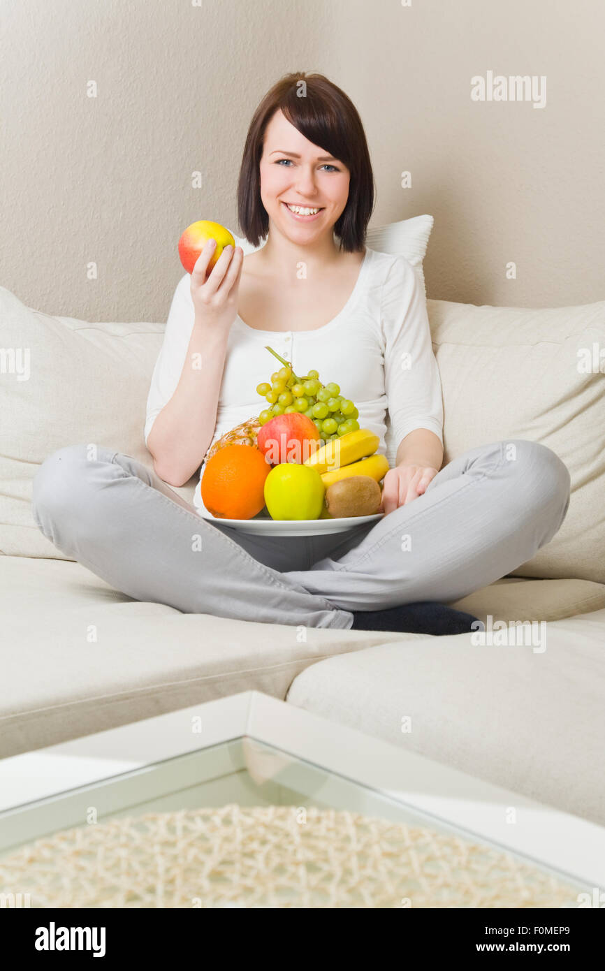 Young woman sitting cross-legged and eating fruits Stock Photo - Alamy
