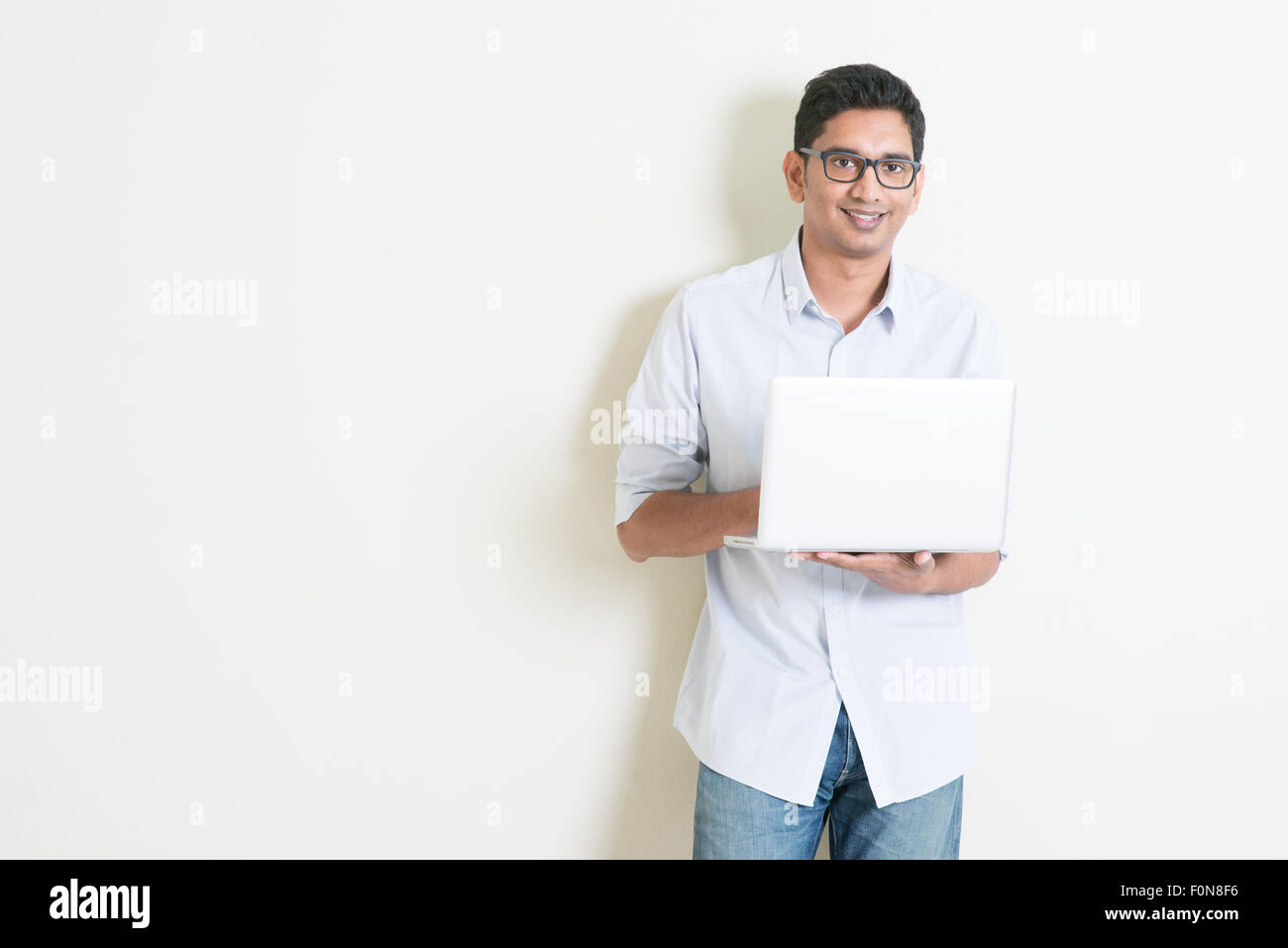 Portrait of handsome casual business Indian guy using laptop computer ...