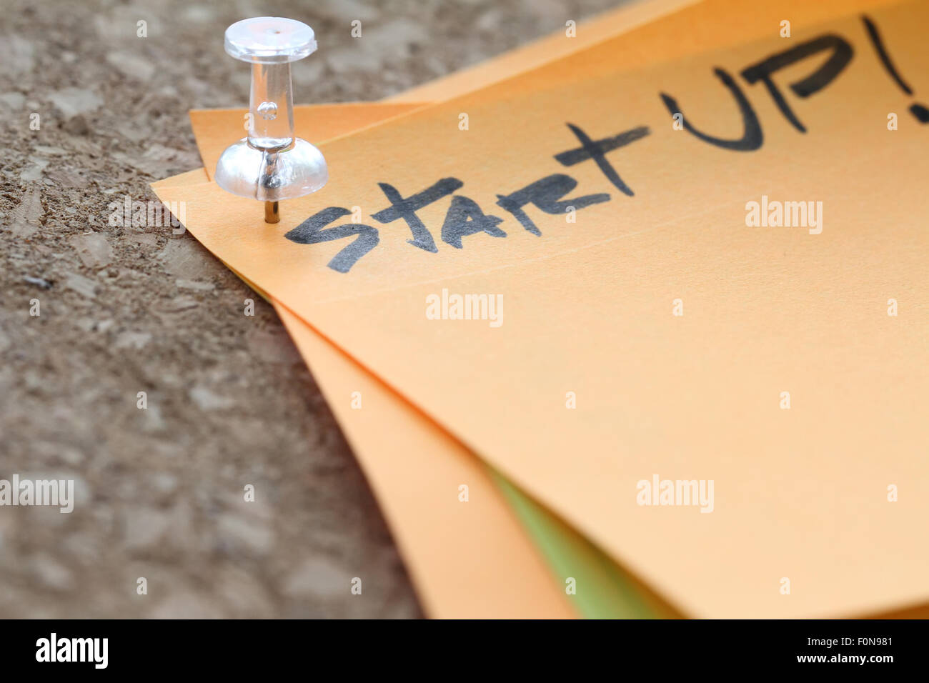 close up on pin and start up word on sticky note with cork board as ...