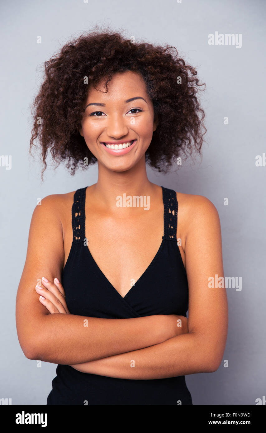 Smiling african woman standing with arms folded on gray background ...