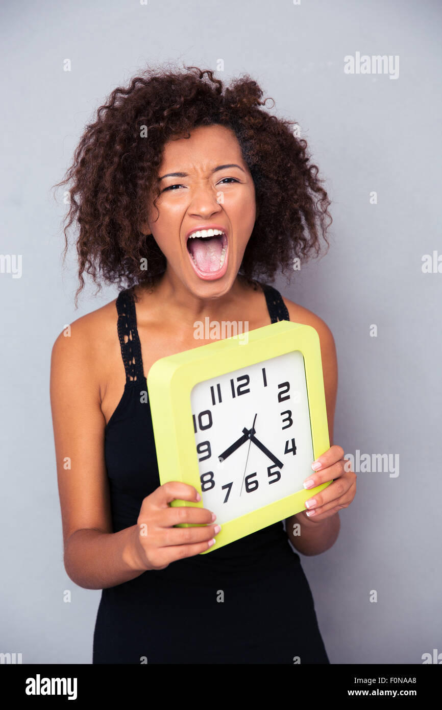 Portrait of african woman holding clock and shouting over gray ...