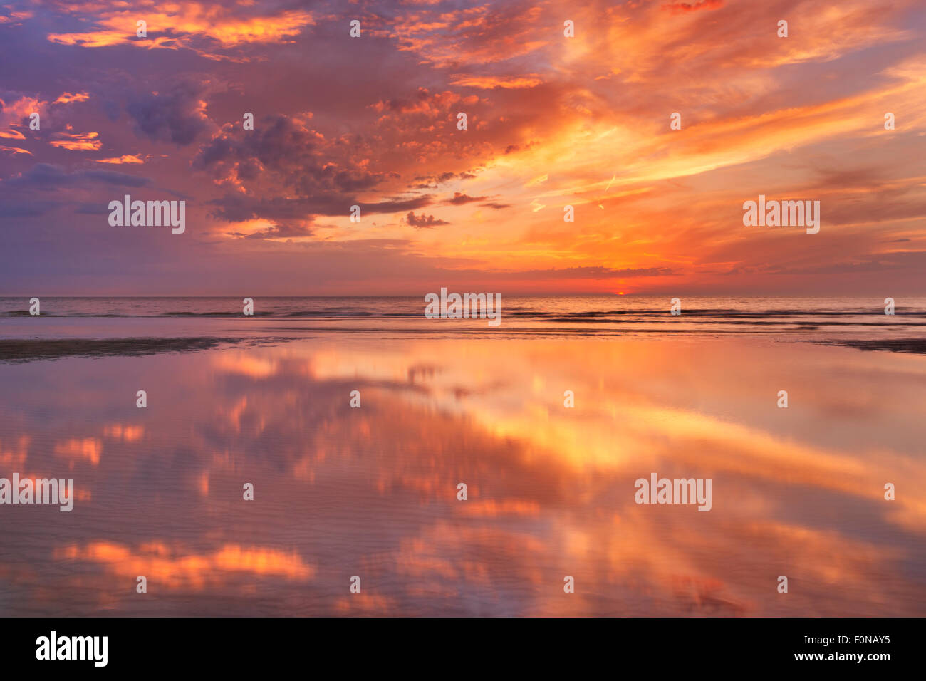 Spectacular sunset colours over sea reflected in the water at low tide ...