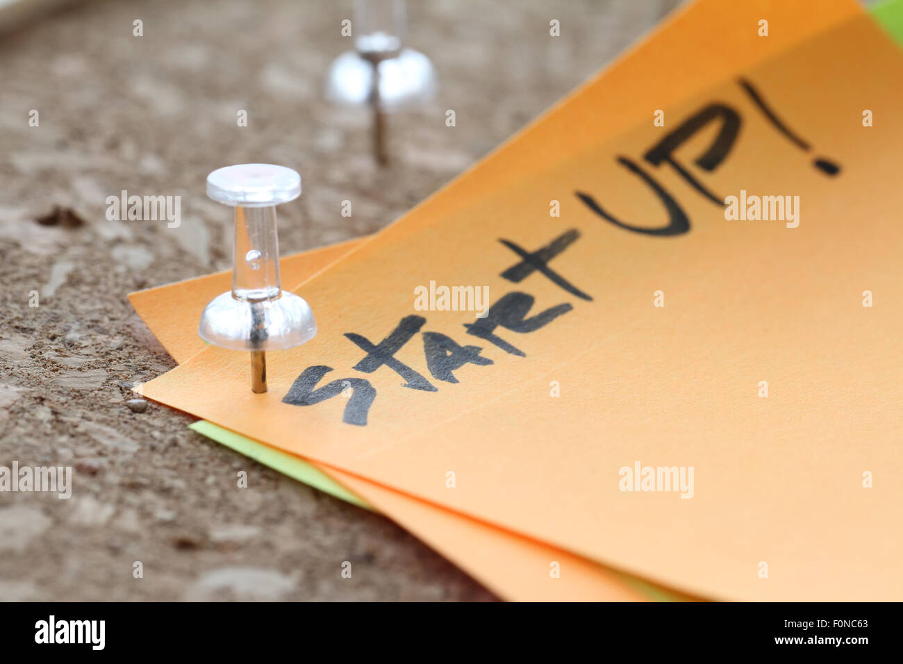 close up on pin and start up word on sticky note with cork board as ...
