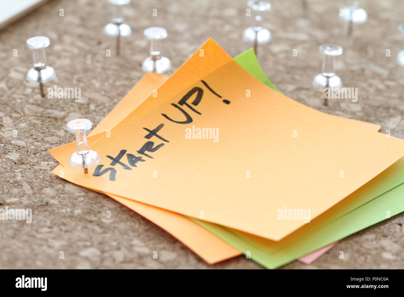 close up on pin and start up word on sticky note with cork board as ...