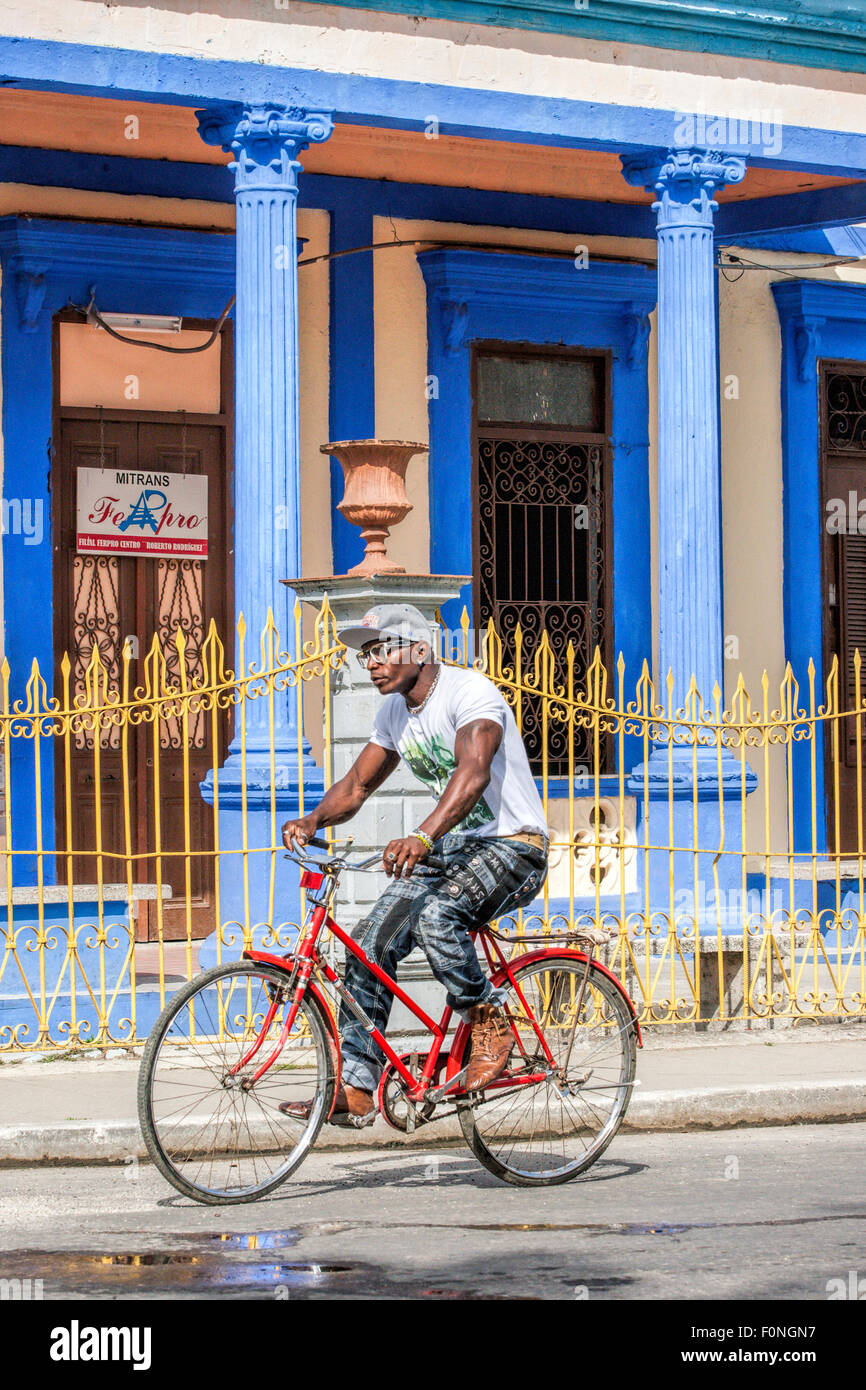 Black Cuban man riding a red bicycle in front of very colourful ...