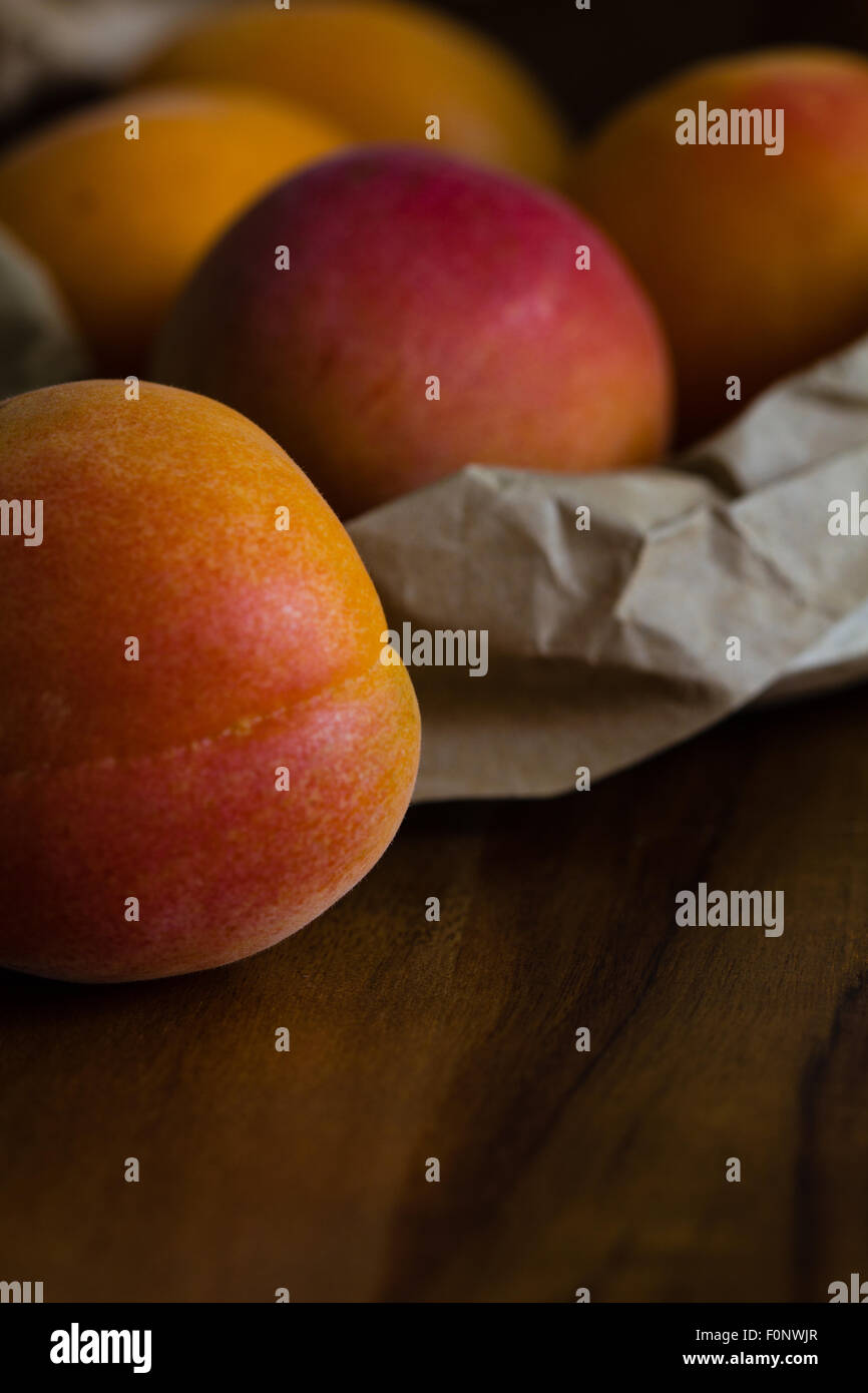 Fresh apricots in a brown paper bag on a wood background with copy ...