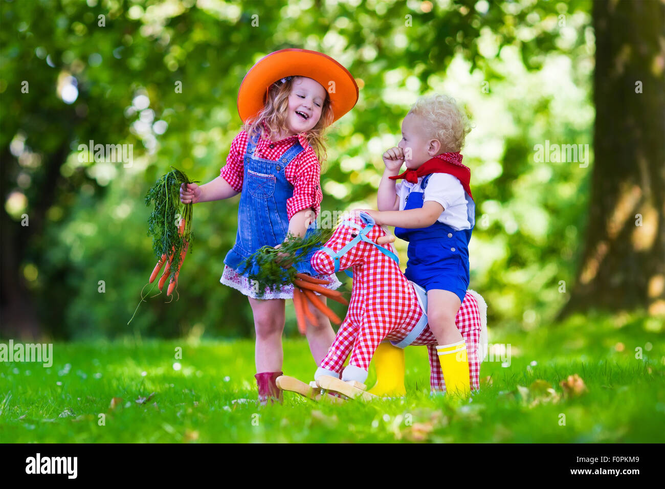 Little boy and girl dressed up as cowboy and cowgirl playing with toy ...